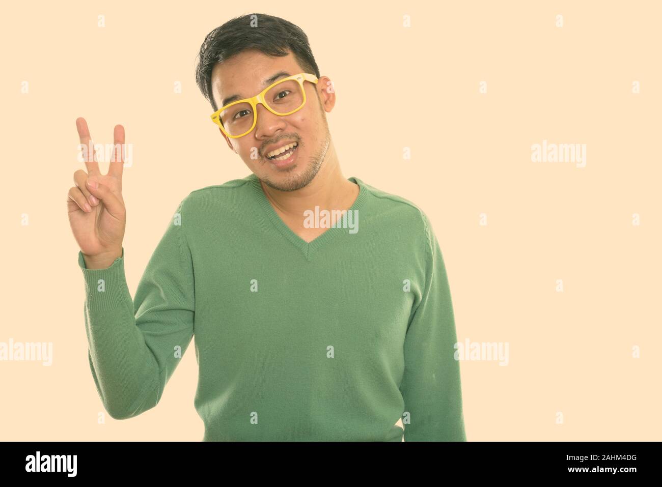 Studio shot of young happy Asian man smiling and giving peace sign ...