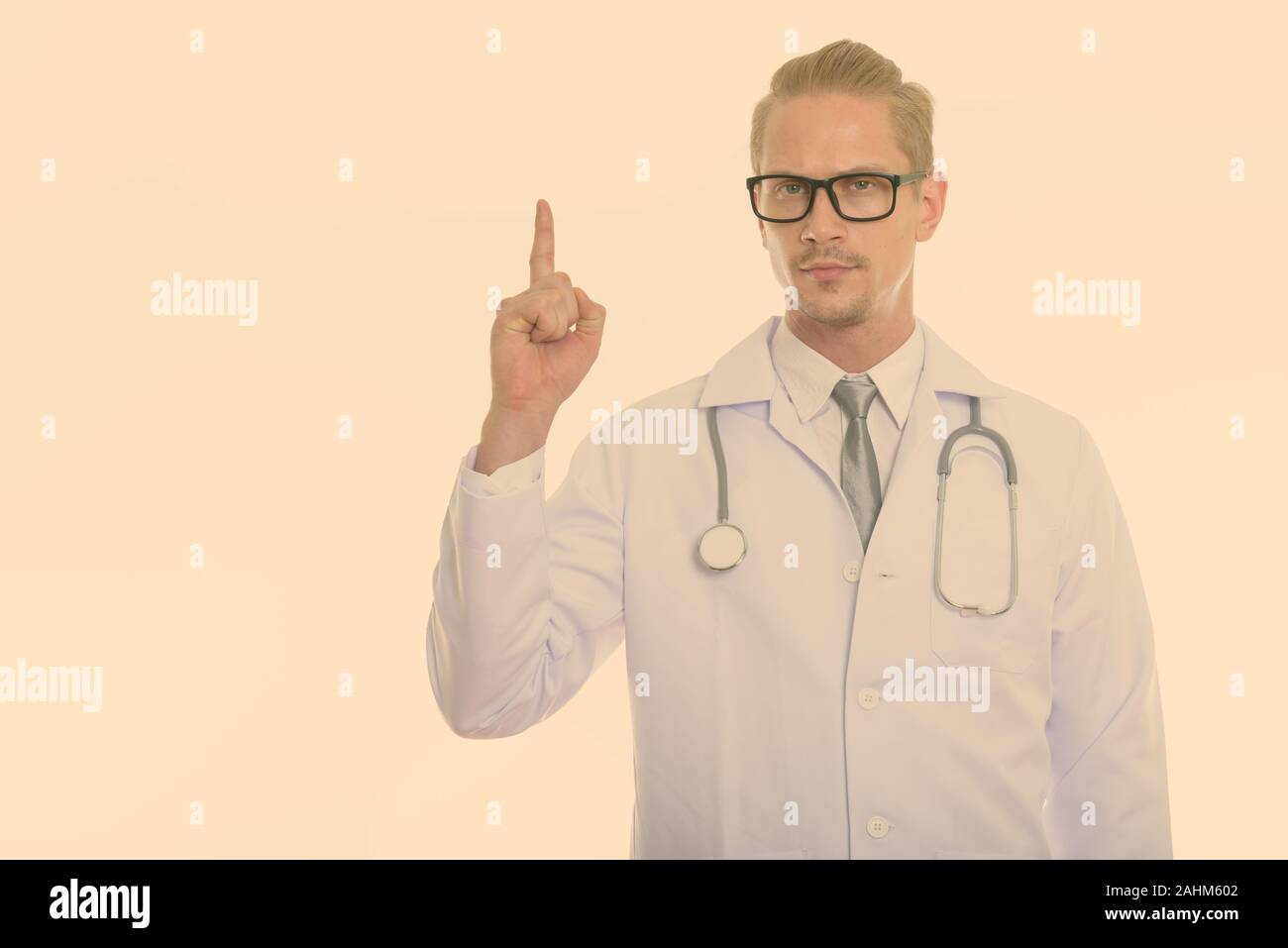 Studio shot of young handsome man doctor pointing finger up Stock Photo ...