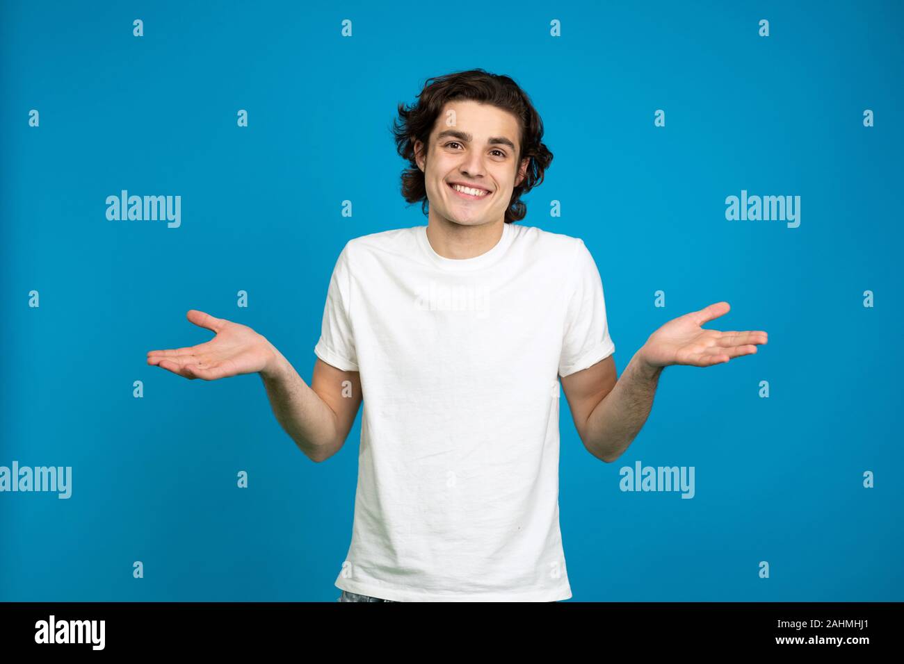 Front view of smiling young man showing shrug gesture isolated on blue ...