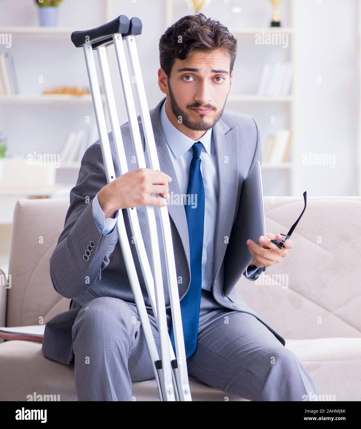 The businessman with crutches and broken leg at home working Stock ...