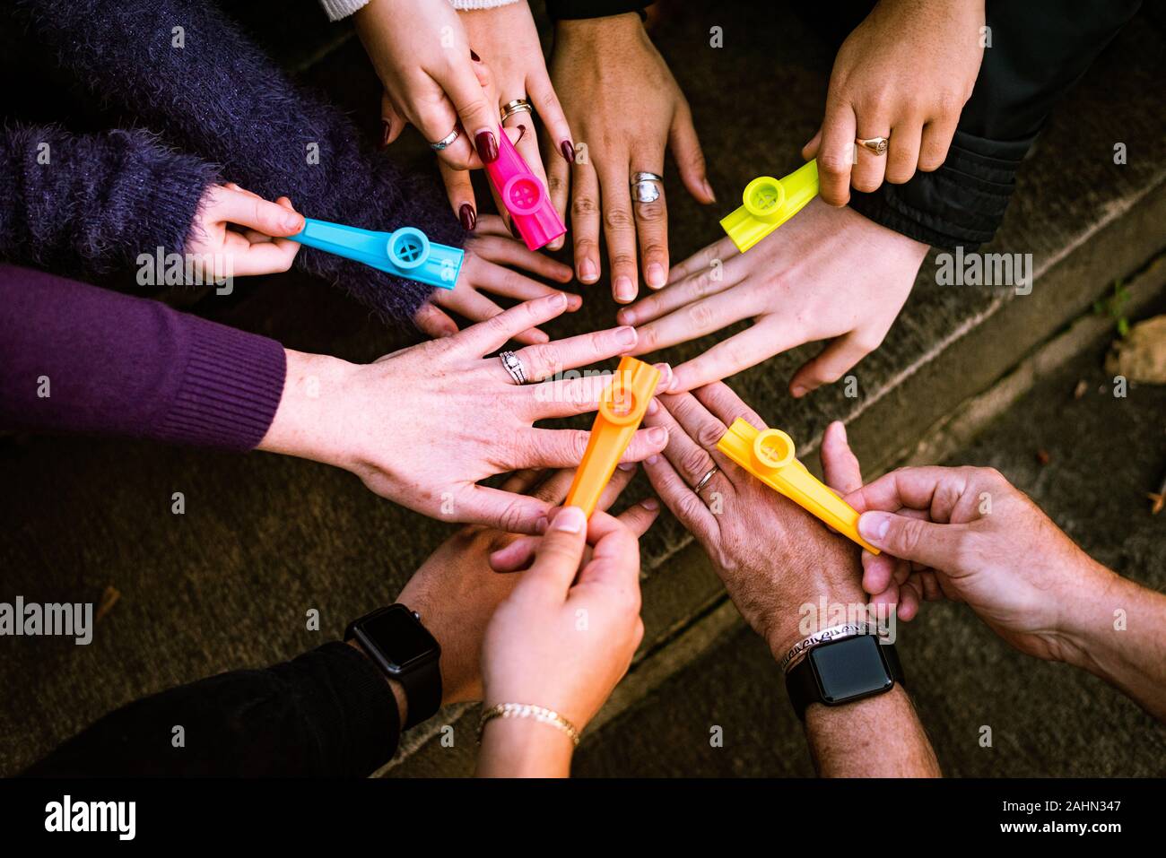 A circle of hands reach in to the center, with some holding musical ...