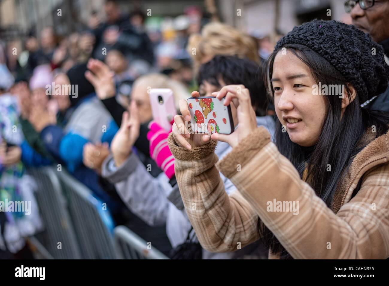 A young Asian-American woman standing in a crowd recording with an ...