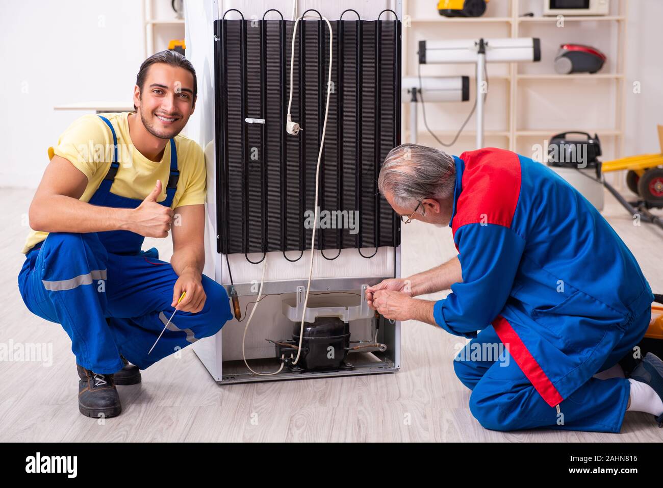 The two contractors repairing fridge at workshop Stock Photo - Alamy