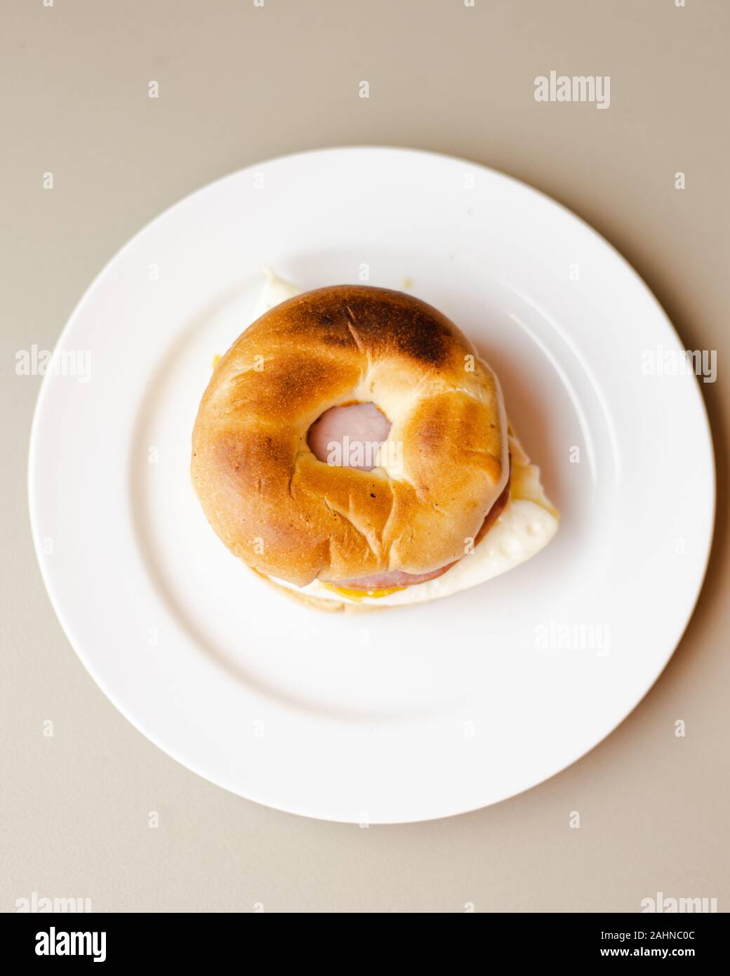 top down shot of egg bacon bagel breakfast sandwich on a white plate ...