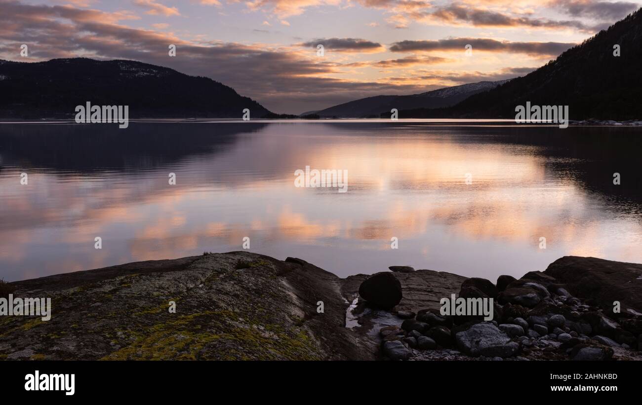 Saturated sunset sky reflected on still, calm fjord lake during a ...