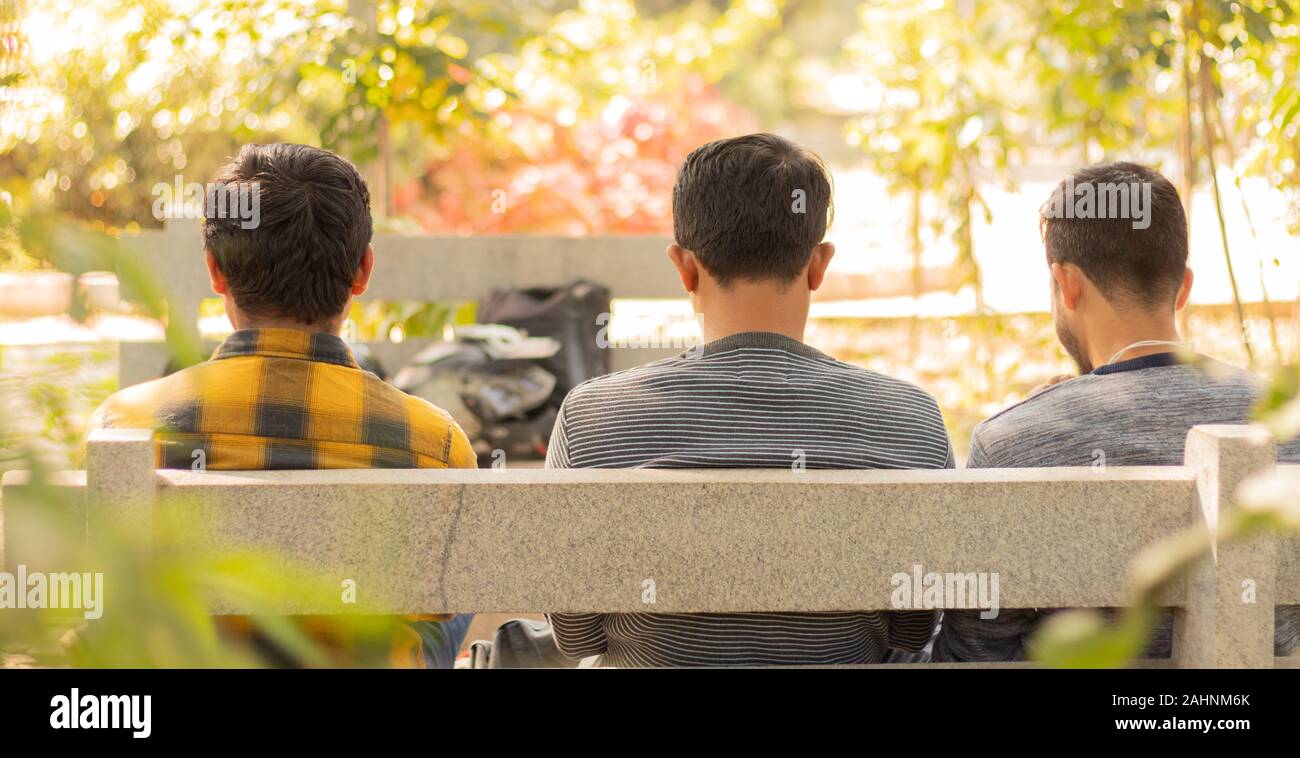 Back view of three friends sitting on table busy on mobile at park ...
