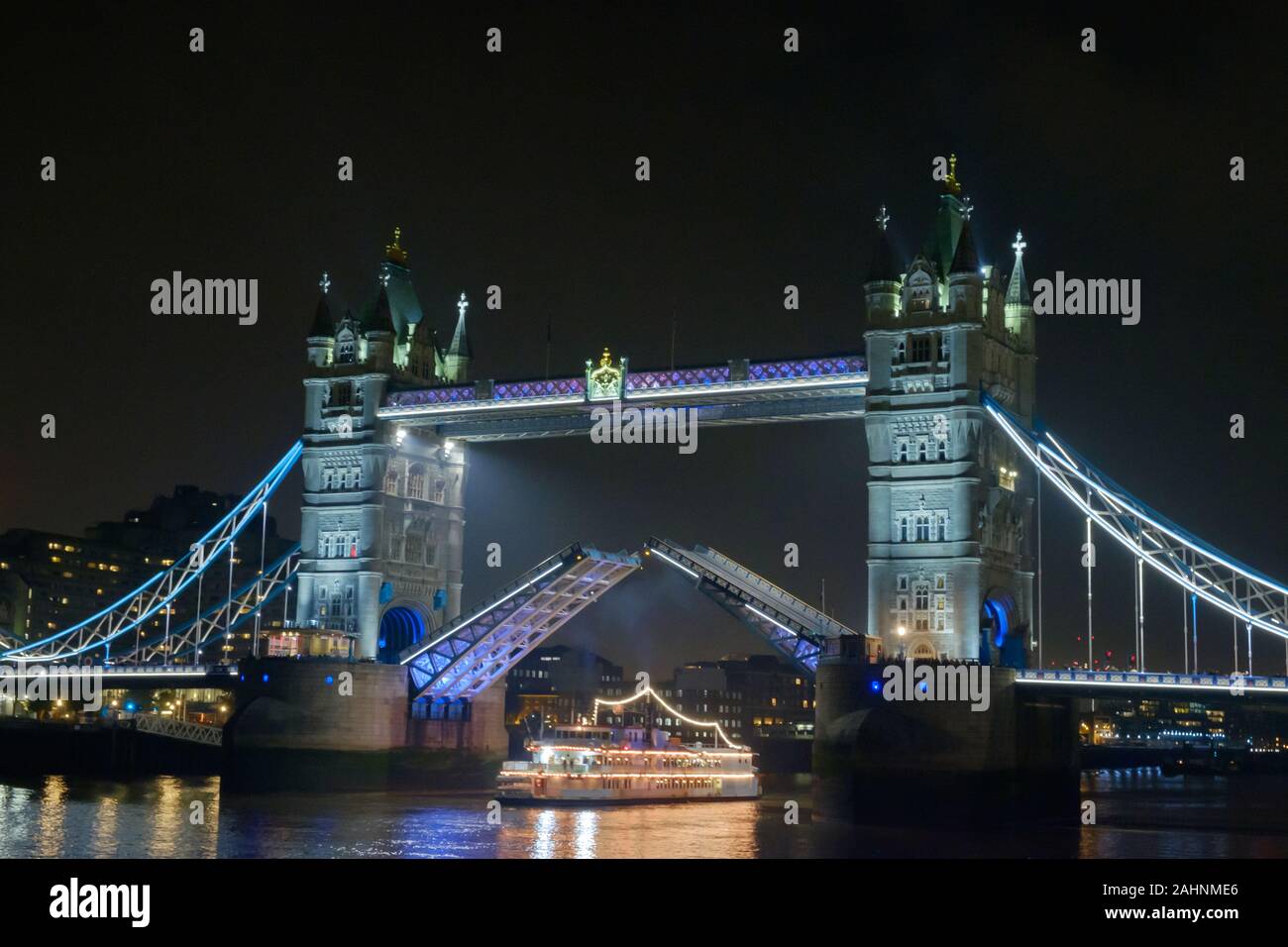 Iconic Tower Bridge lit up at night, lifting to allow brightly lit ...