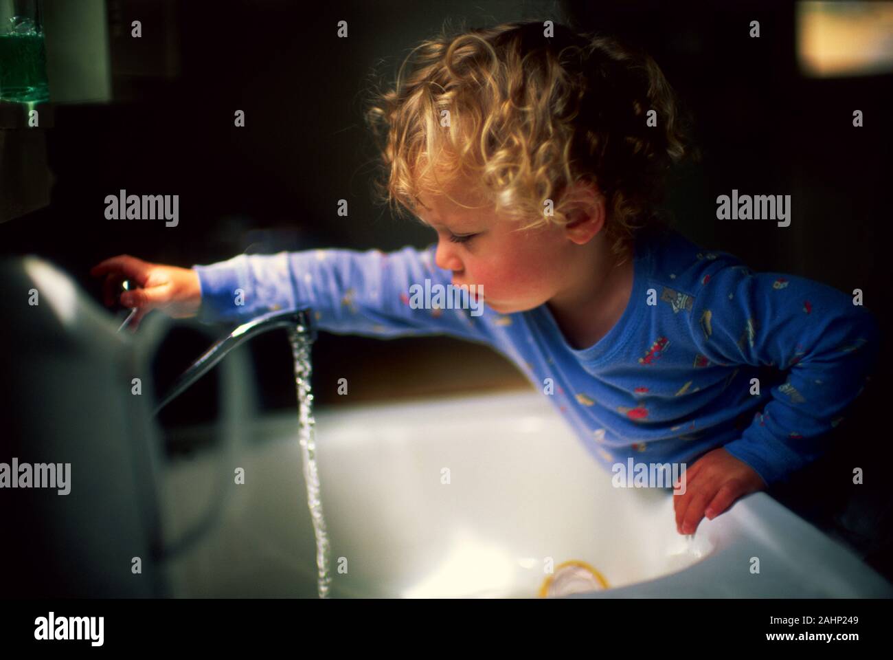 Side view of a little boy opening a tap Stock Photo - Alamy