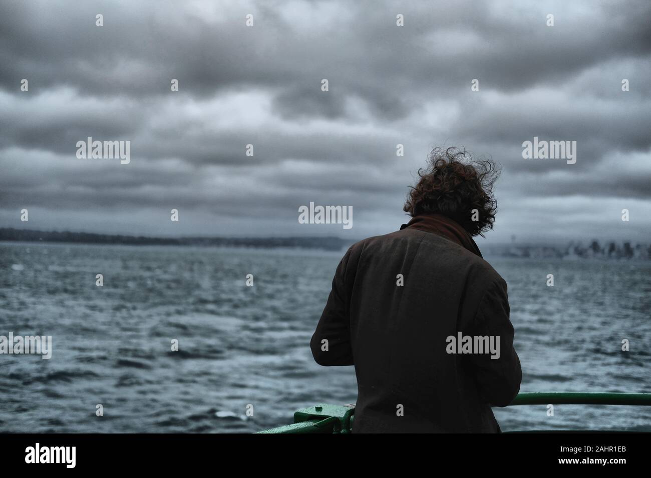 Young man overlooking the ocean with coastline land in the horizon ...
