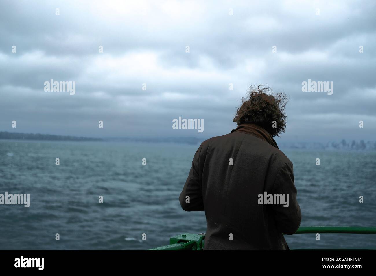 Young man overlooking the ocean with coastline land in the horizon ...
