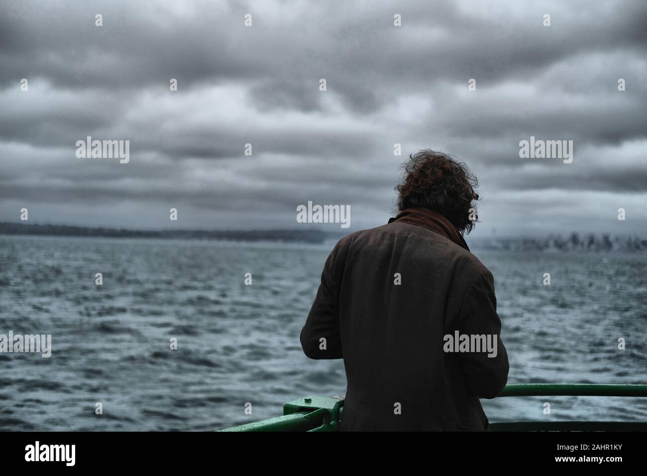 Young man overlooking the ocean with coastline land in the horizon ...