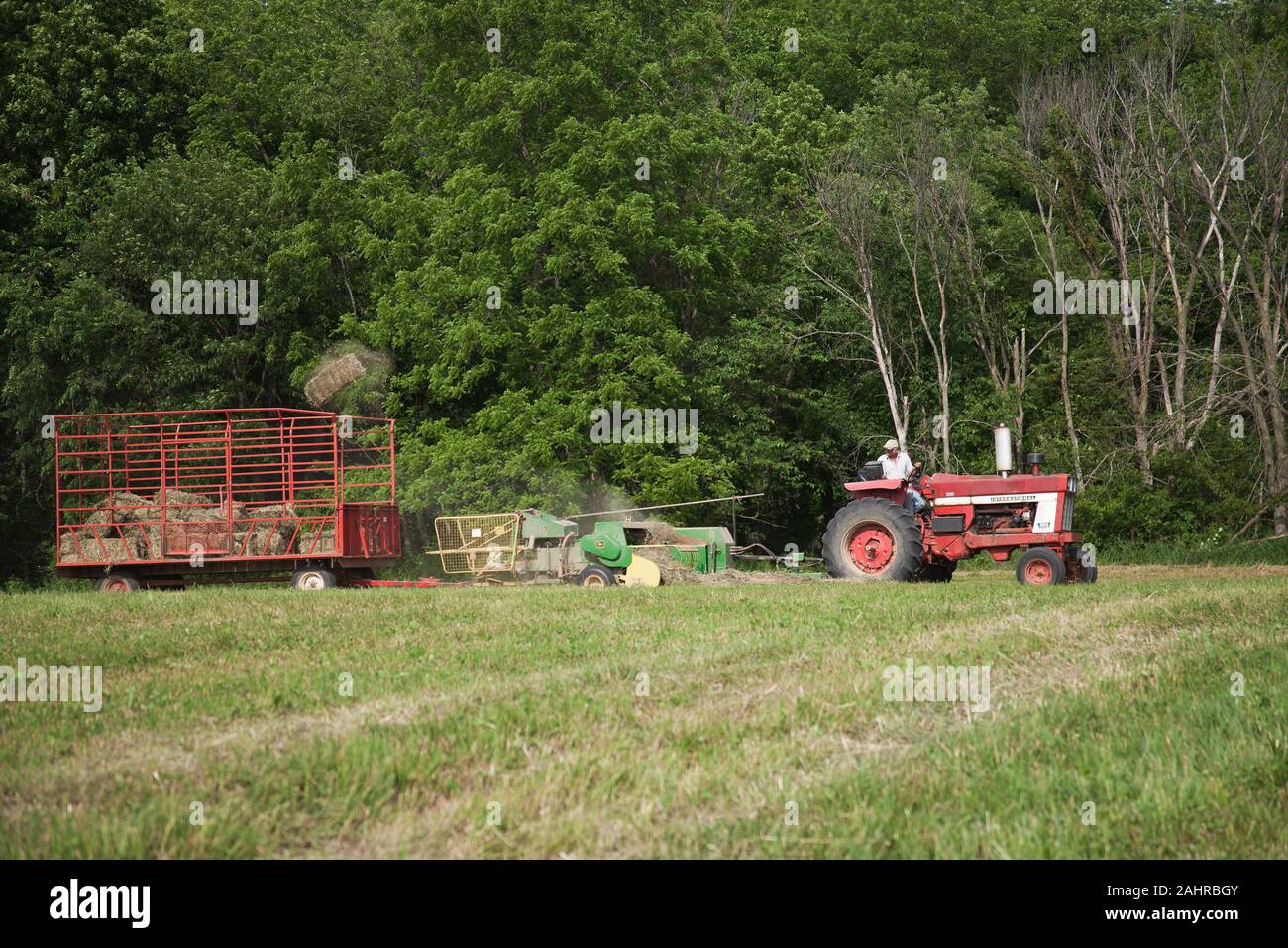 Man on International Harvester Farmall tractor, baling hay in a field ...