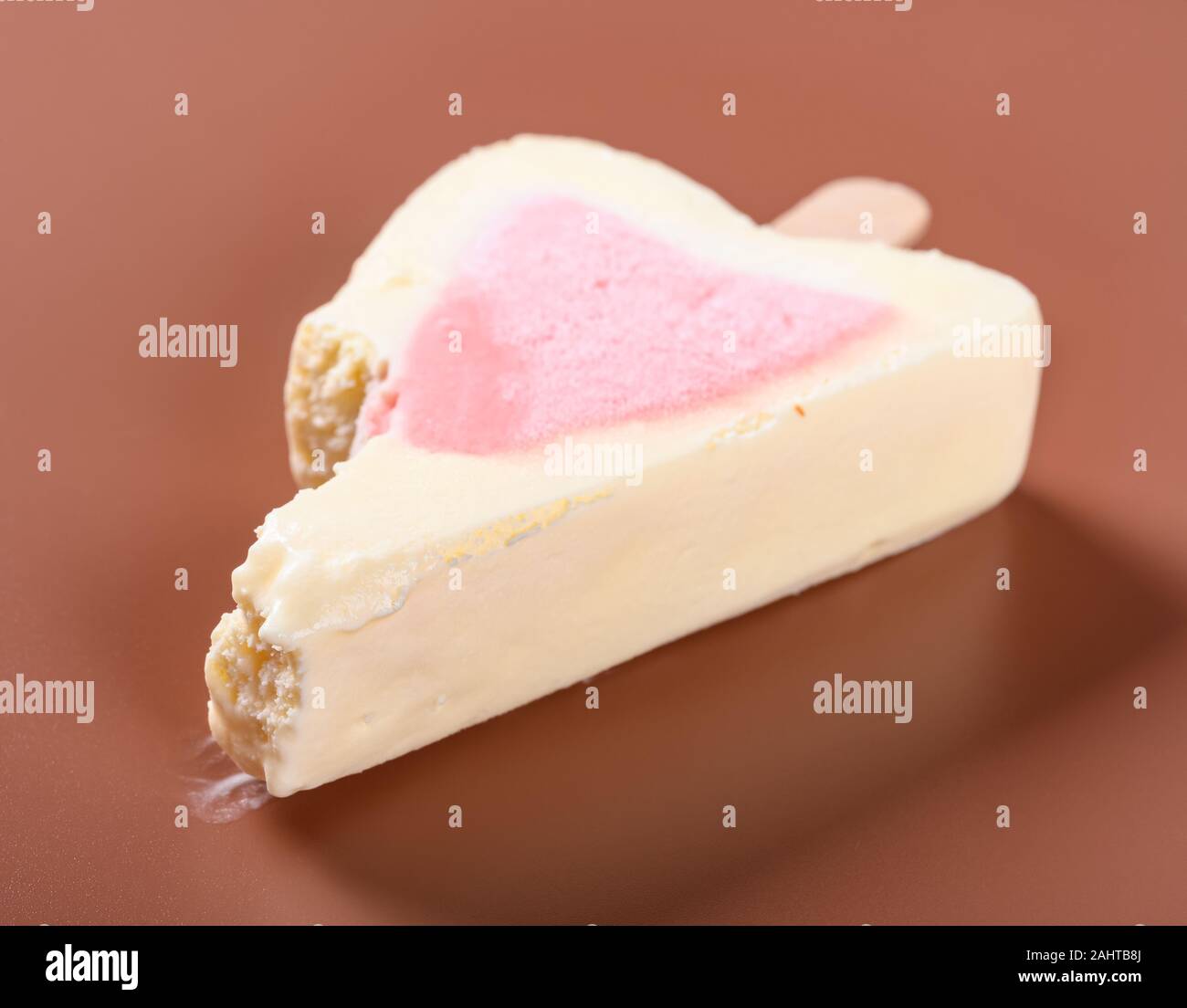 side view half eaten strawberry flavor popsicle on a brown background ...