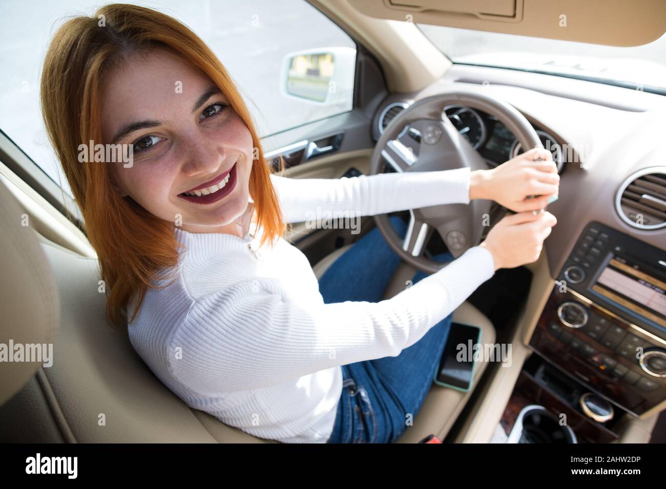 Young redhead woman driver behind a wheel driving a car smiling happily ...