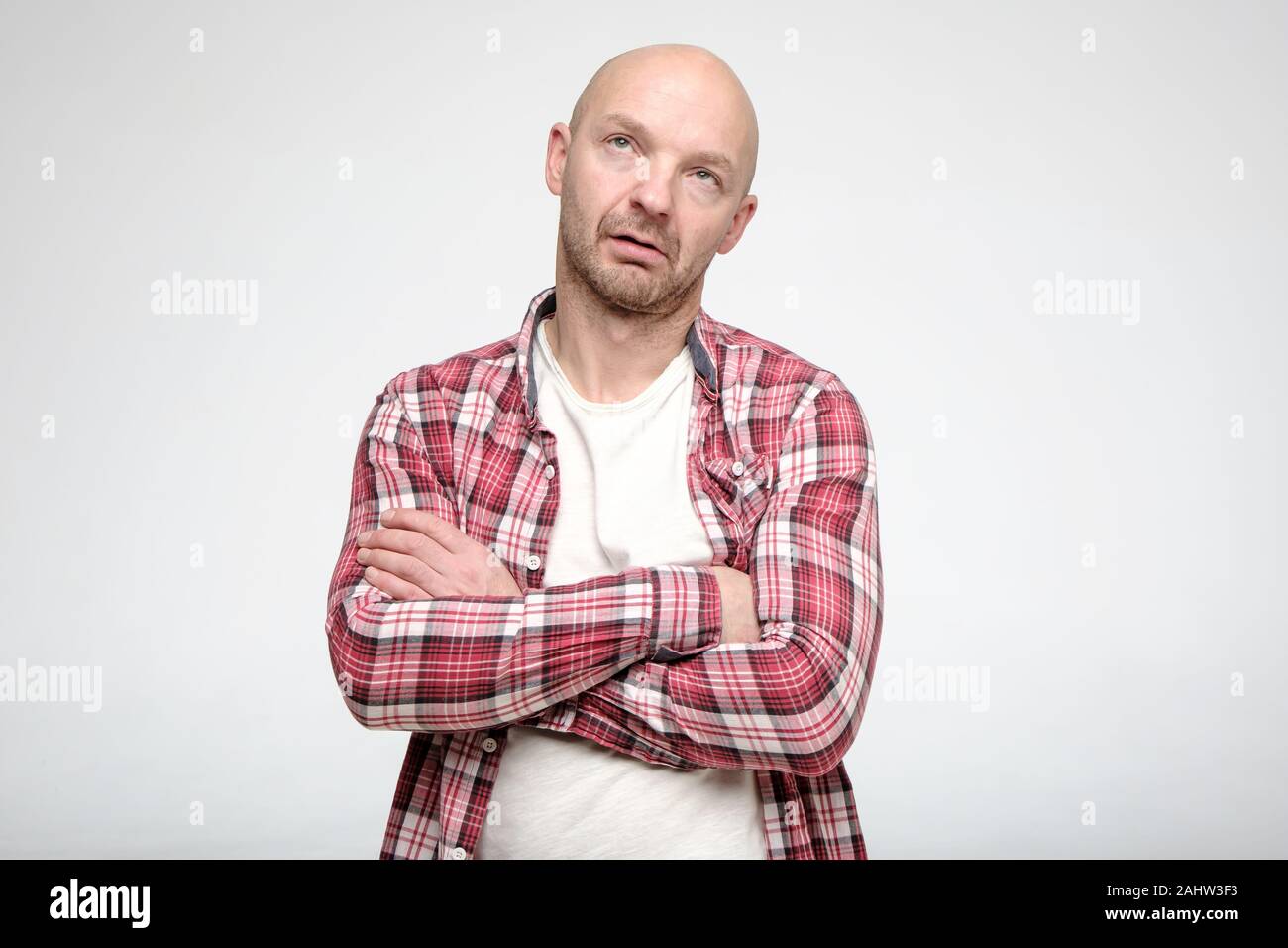 Bald man with a silly expression on his face is standing with his arms ...