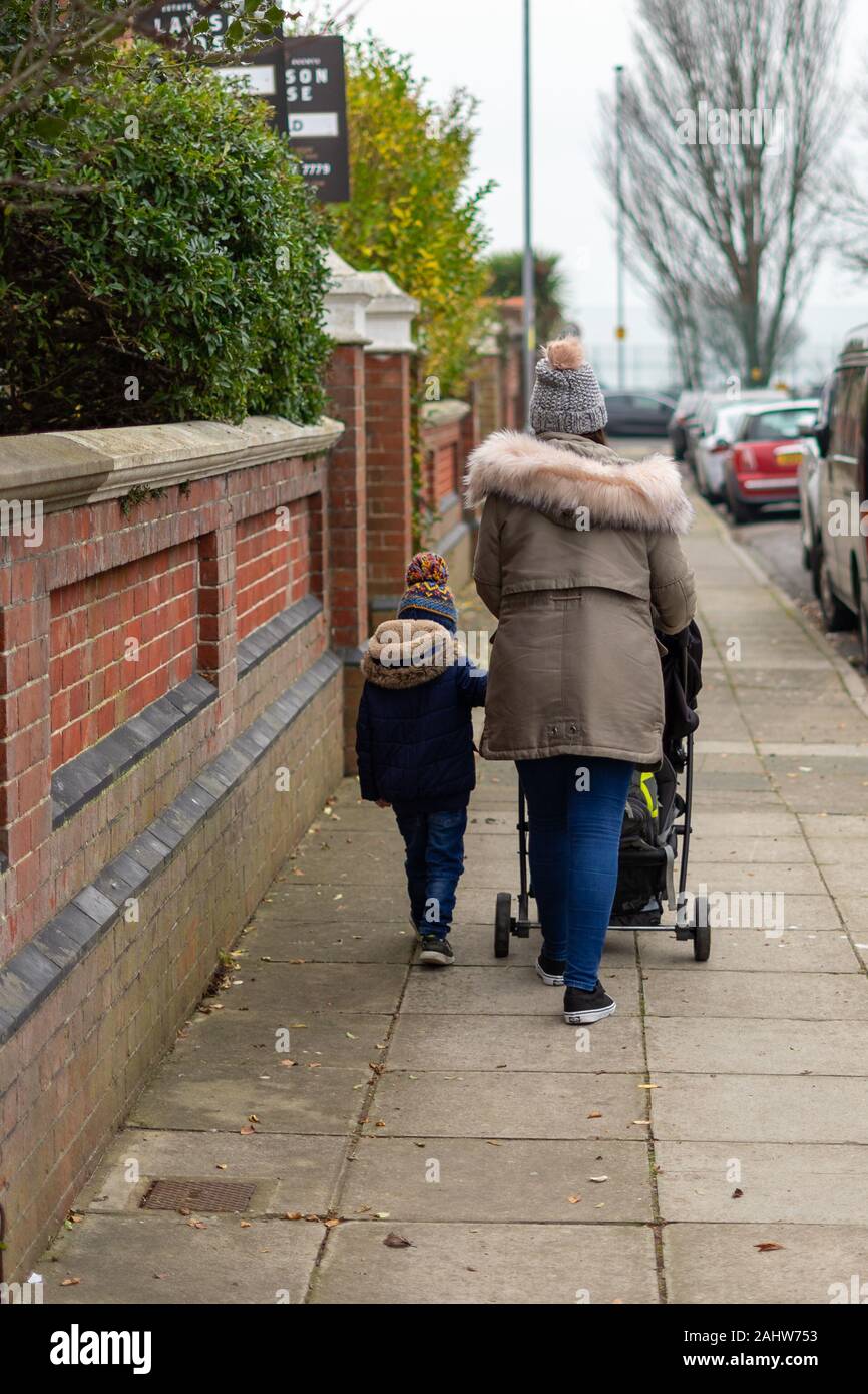 A mother pushing a pram, pushchair or stroller down a street while a ...