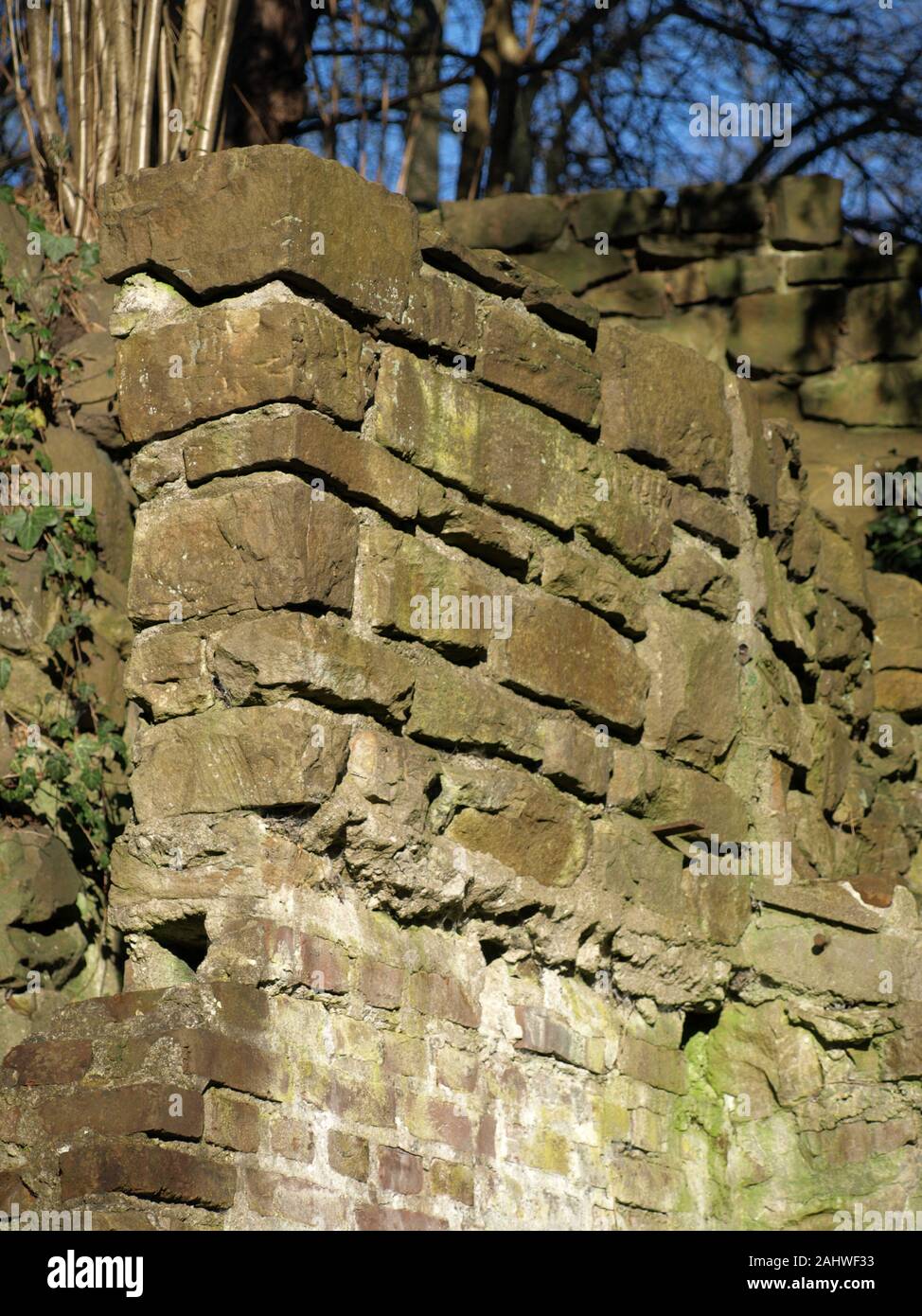 old quarry stone wall with a foundation of bricks. Blue sky and trees ...