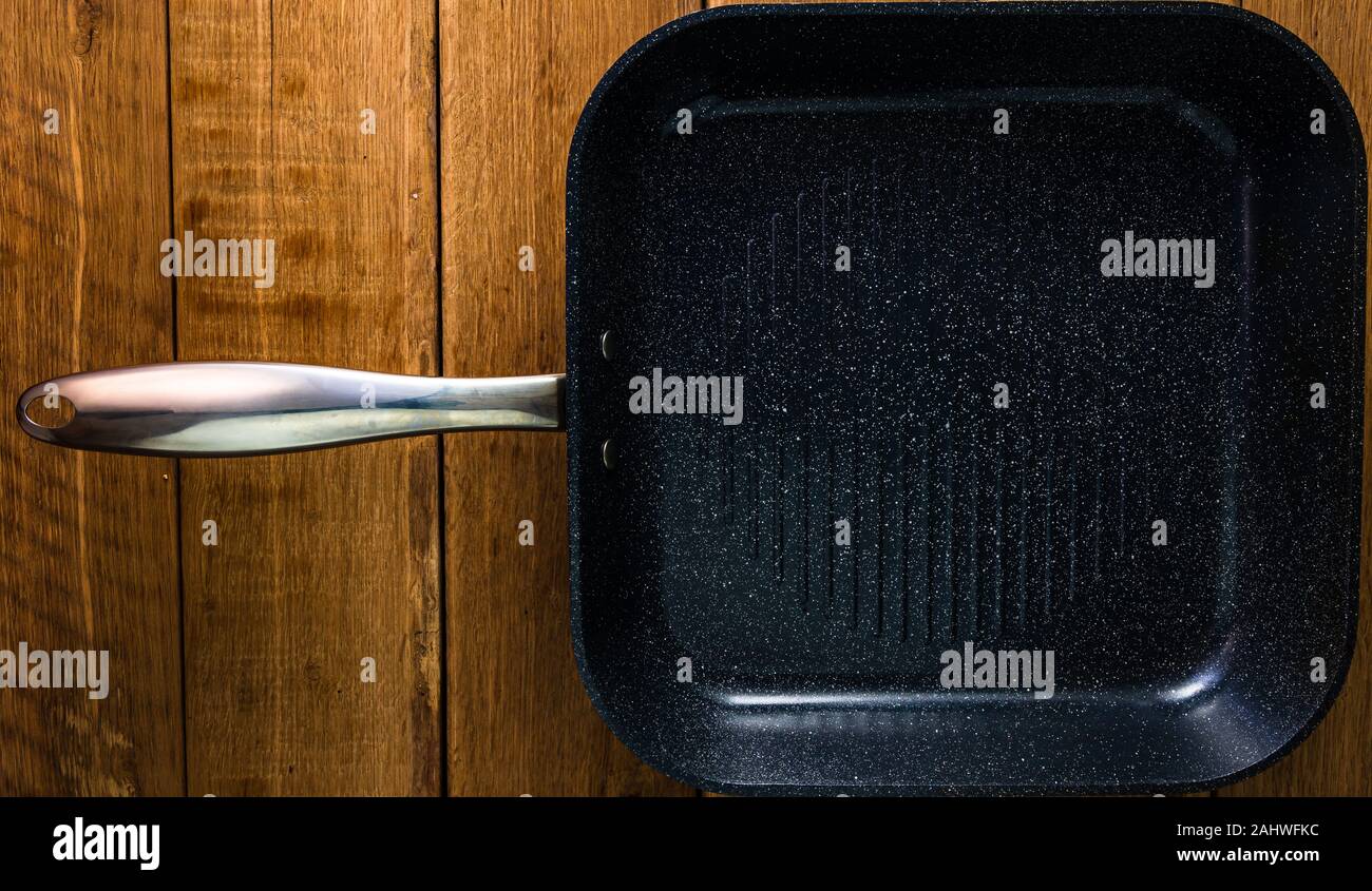 Black frying pan, grill over wooden table, top view, copy space ...