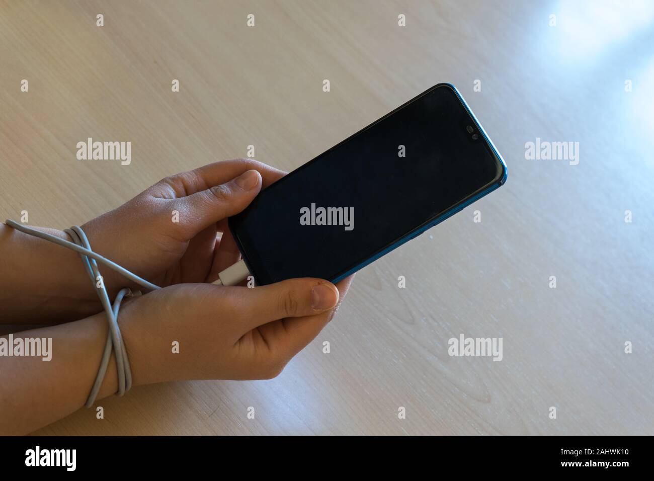 Woman's hands tied to the smartphone by the battery charging wire ...