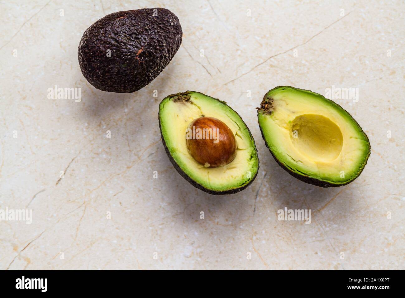 Avocado pear open, stone in one half, and whole avocado, on marble ...