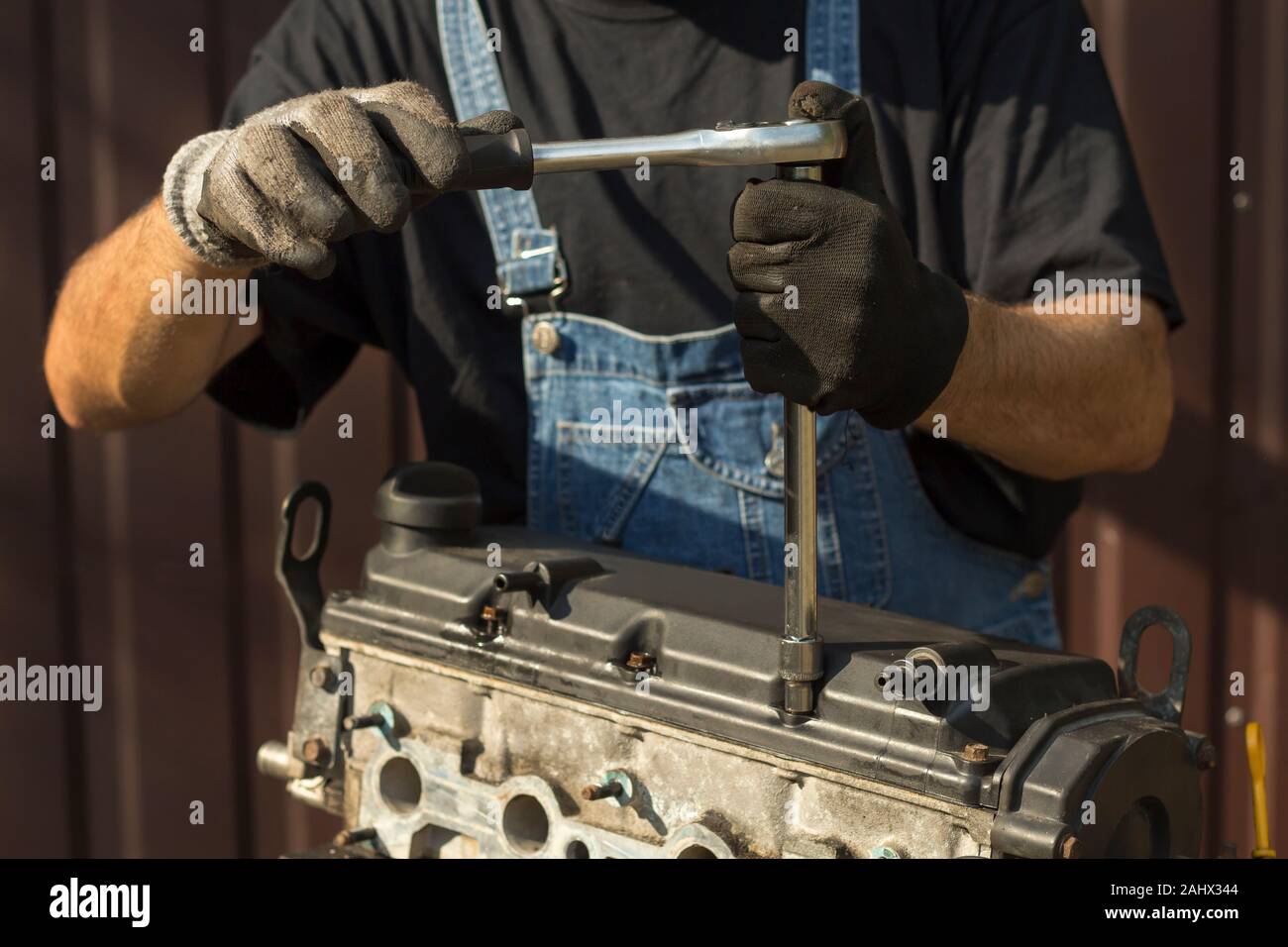A car mechanic in a work suit unscrews the screws on the engine ...