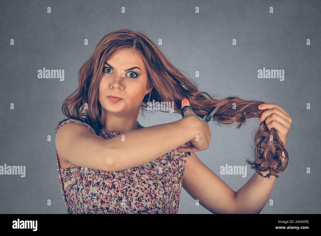 Frustrated woman holding her hair and scissors about to cut her hair looking at you camera angry ...