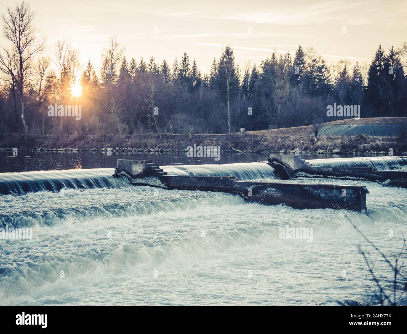 Water flowing over a weir during sunset with sun rays in the winter ...