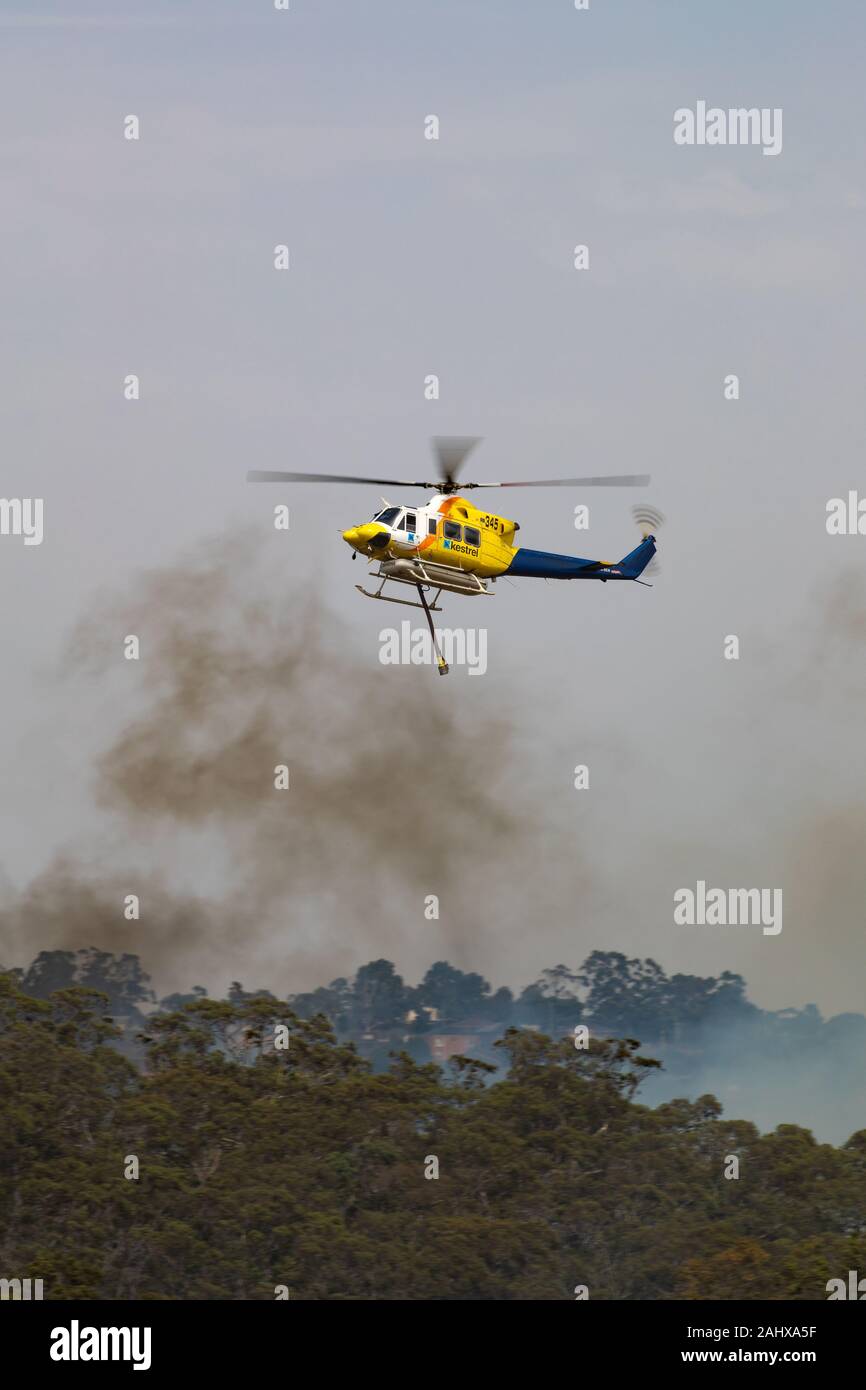 Bell 412 helicopter flying against plumes of smoke while fighting bush ...
