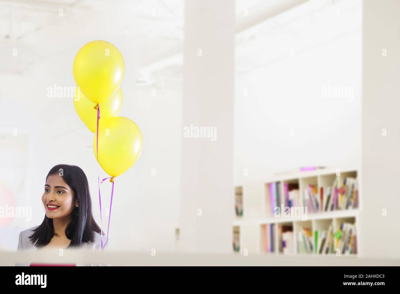 Young woman standing with helium balloons in the office Stock Photo - Alamy
