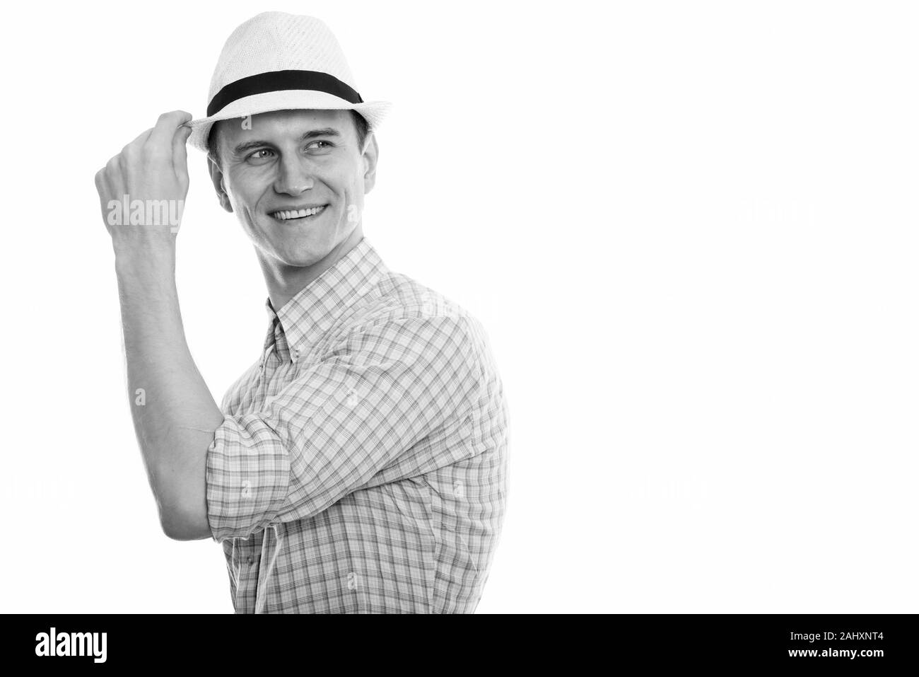 Thoughtful young happy man smiling while looking back and holding hat ...