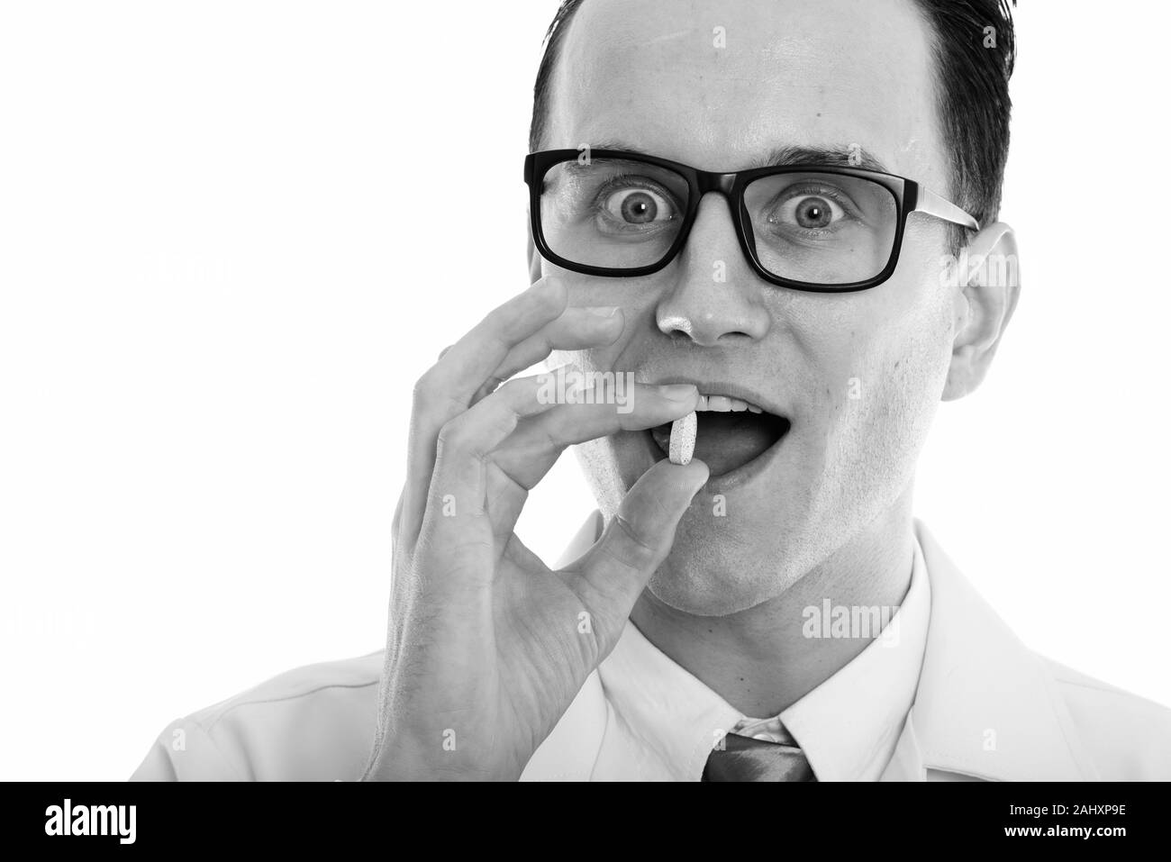 Studio shot of young happy man doctor smiling while eating vitamin ...