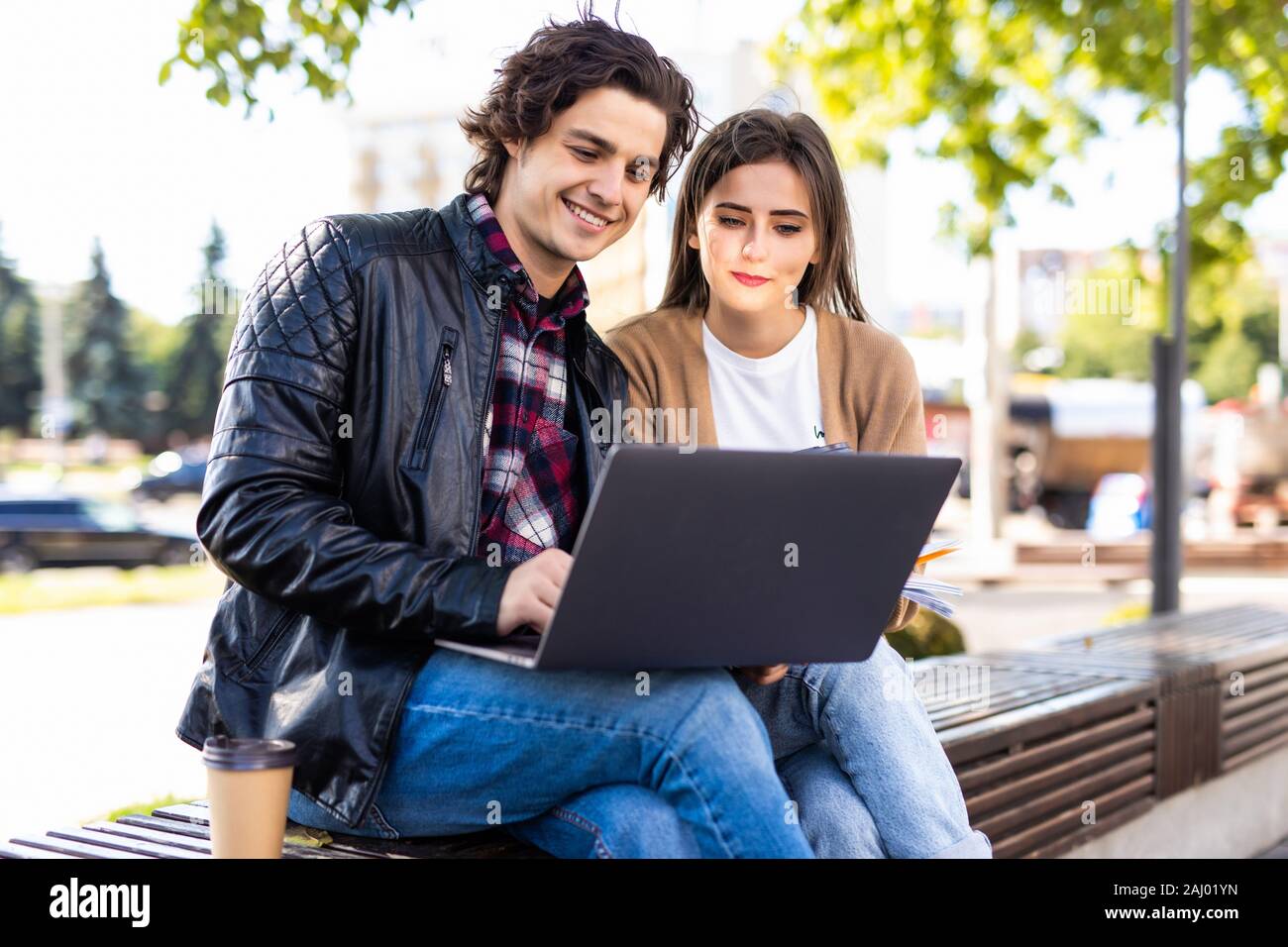 Happy young couple using laptop computer sitting on bench in city ...