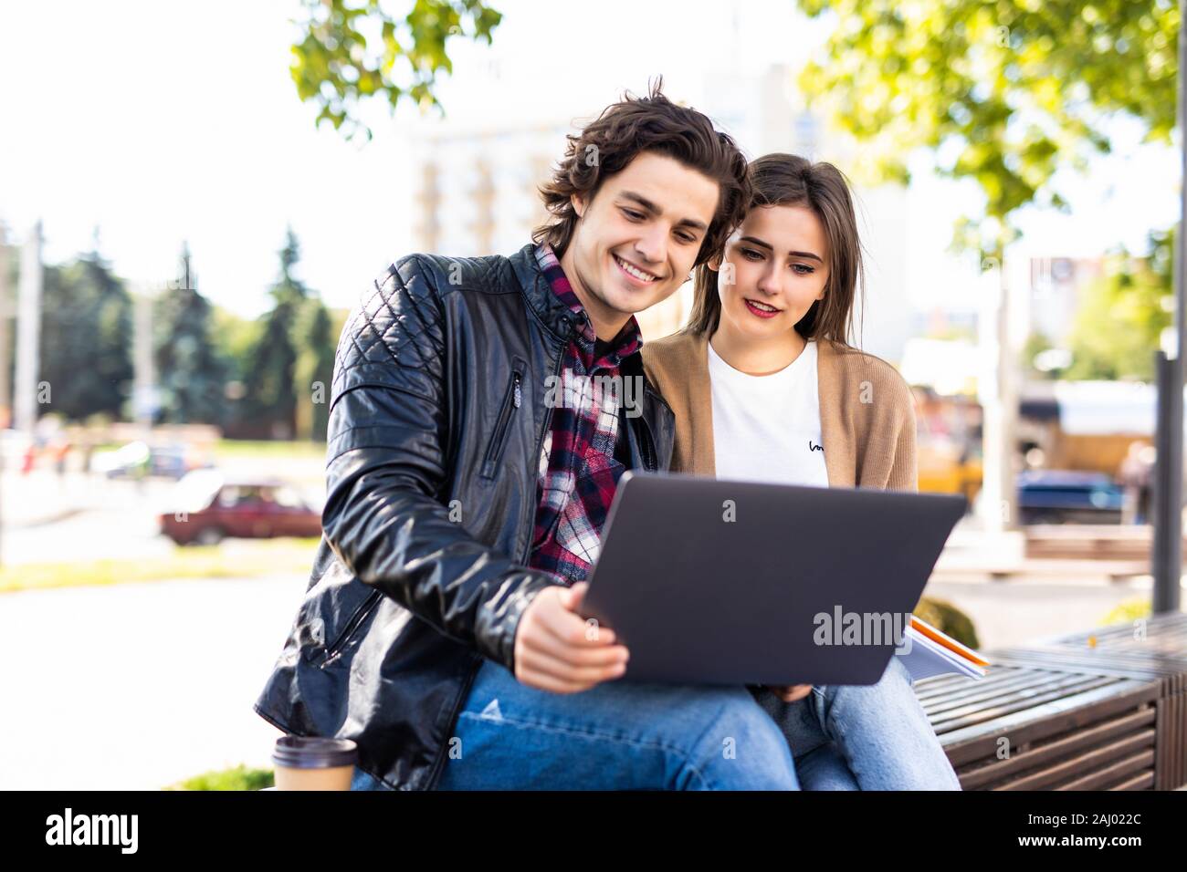 Happy young couple using laptop computer sitting on bench in city ...
