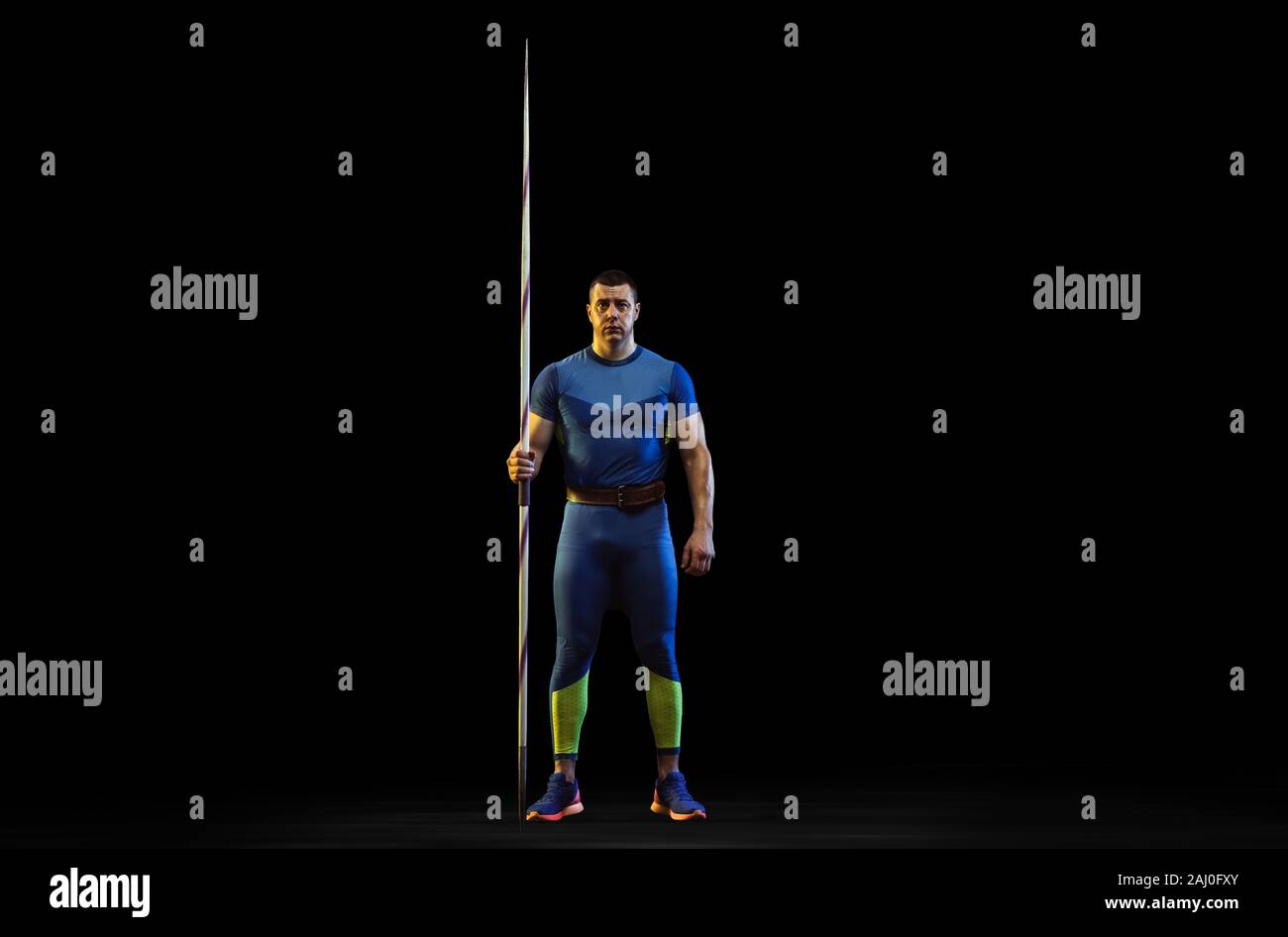 Male athlete practicing in throwing javelin on black background in neon ...
