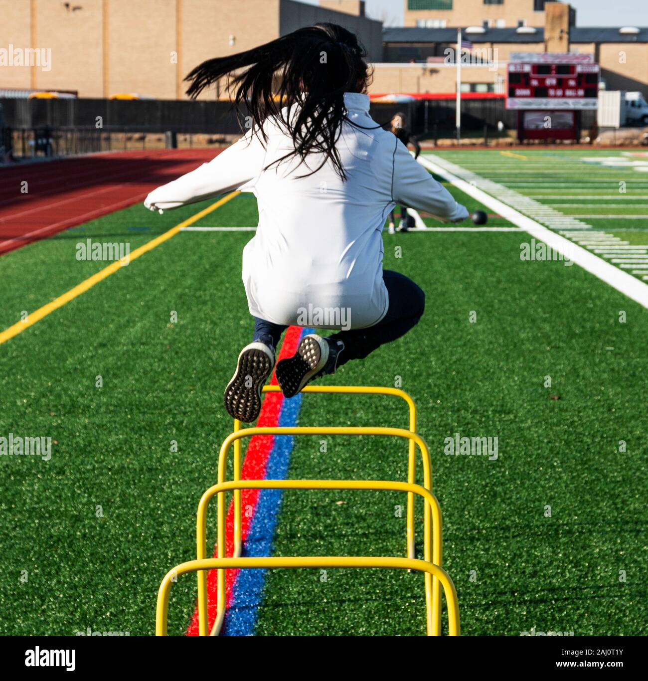 High school teenage girl jumping over two foot yellow hurldes that are ...
