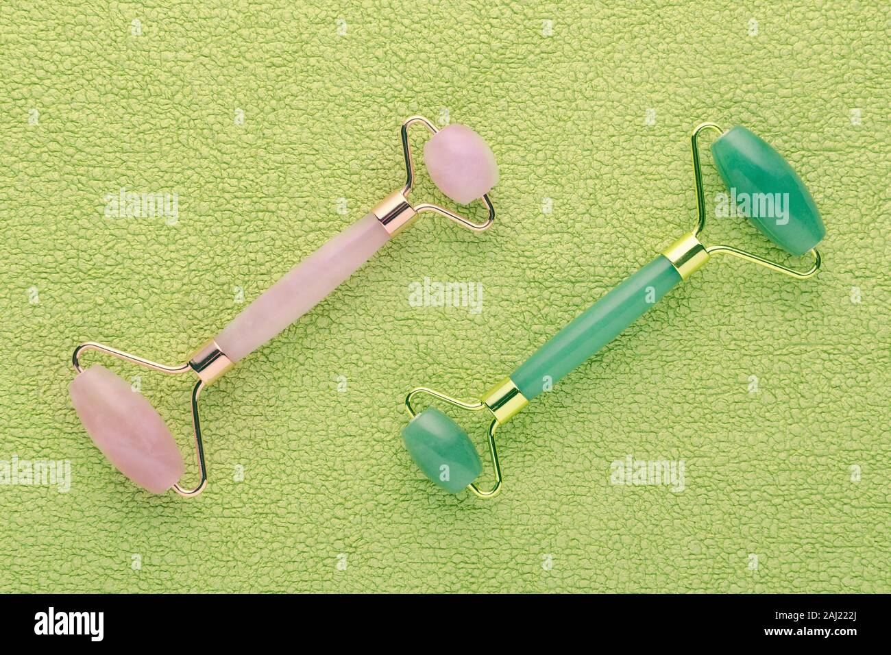real jade facial roller and rose quartz on green background, flat lay ...