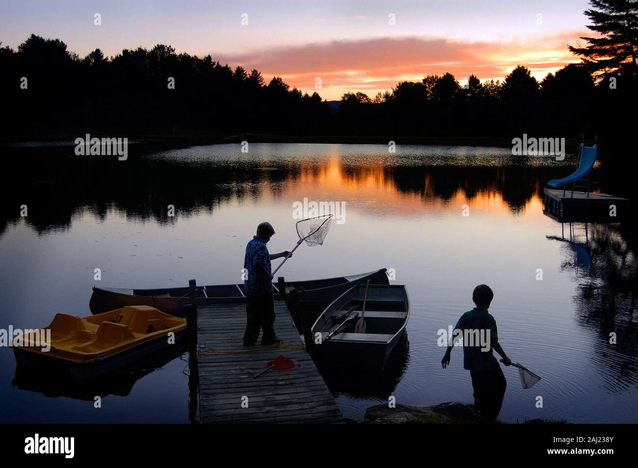Sunset over a pond with two boys' silhouettes against the background ...
