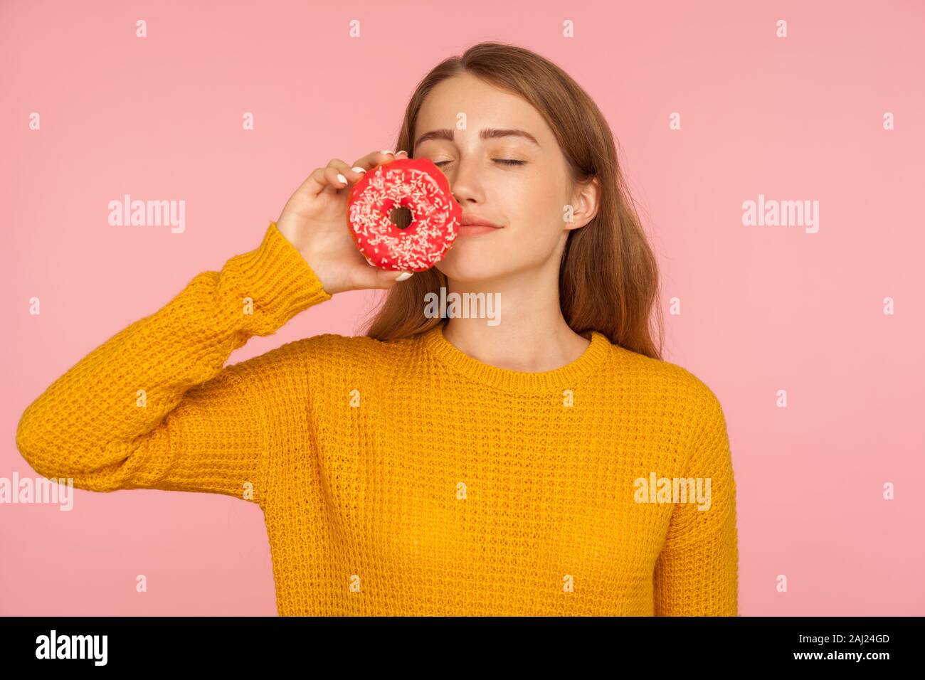 Portrait of fascinating hungry ginger girl in sweater smelling doughnut ...