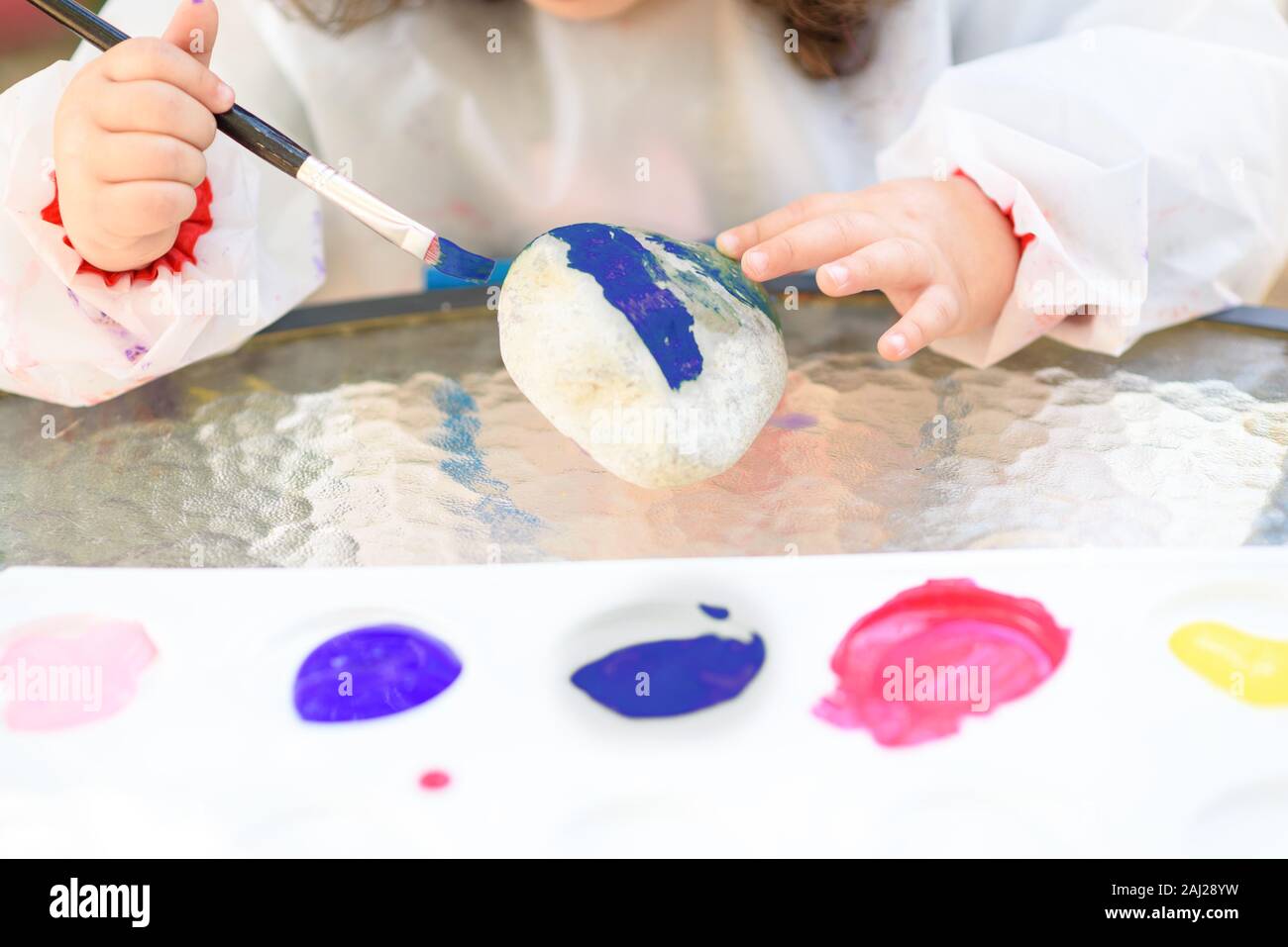 Close-up child hands painting on stone with blue color of the year 2020 ...