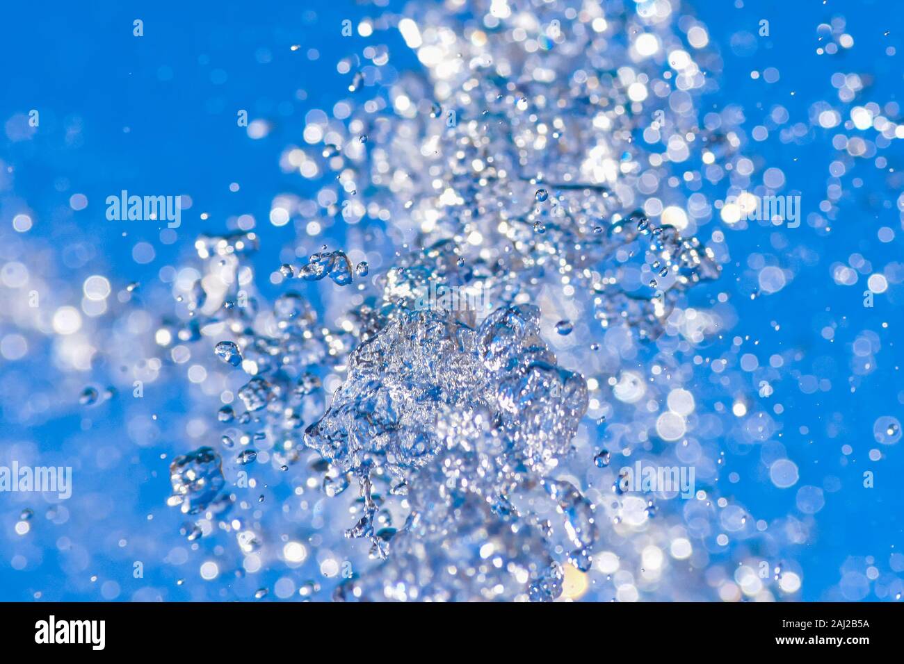 Water droplets spraying from a fountain in abstract design on blue sky ...