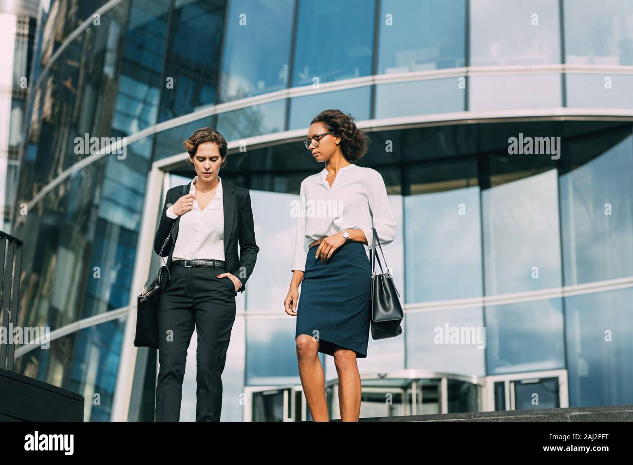 Two colleagues walking down the steps and talking near an office ...