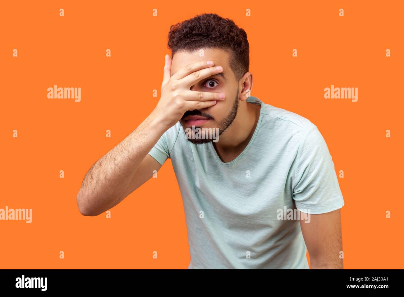 Portrait of curious brunette man with beard in white t-shirt covering ...