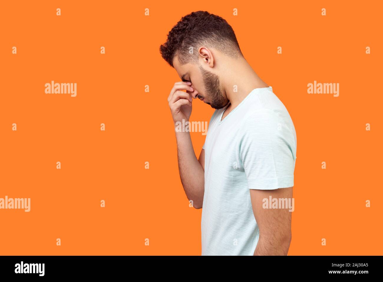 Side view of depressed brunette man with beard in white t-shirt hiding ...
