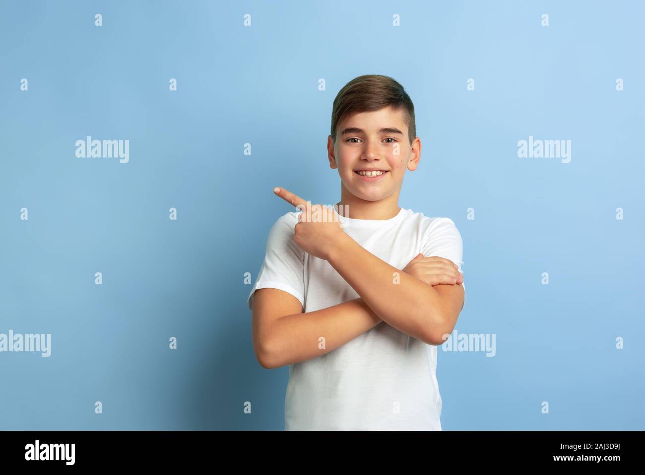 Smiling, pointing at side. Caucasian boy portrait isolated on blue ...