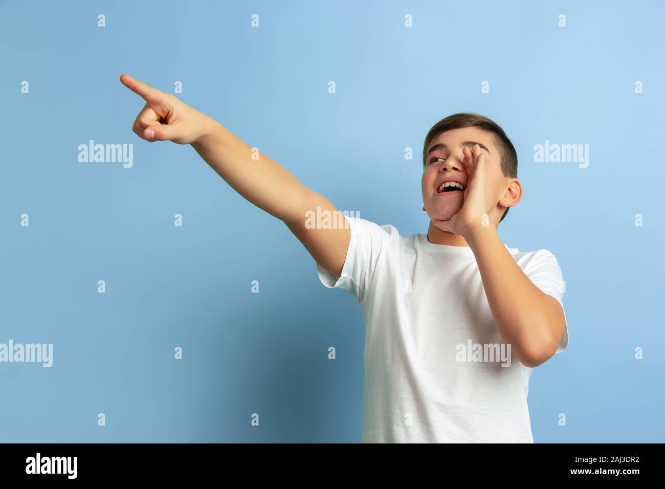 Smiling, pointing at side. Caucasian boy portrait isolated on blue ...