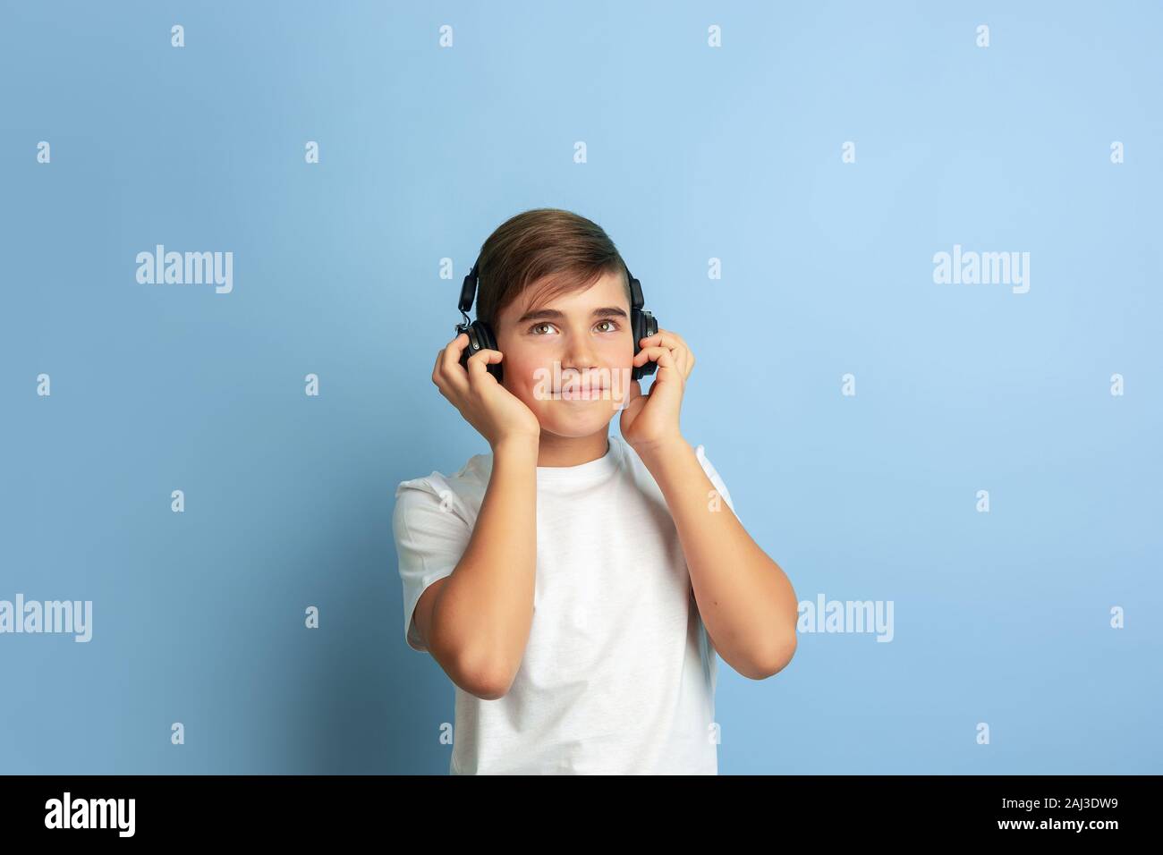 Listen to music, looks joyful. Caucasian boy portrait isolated on blue ...