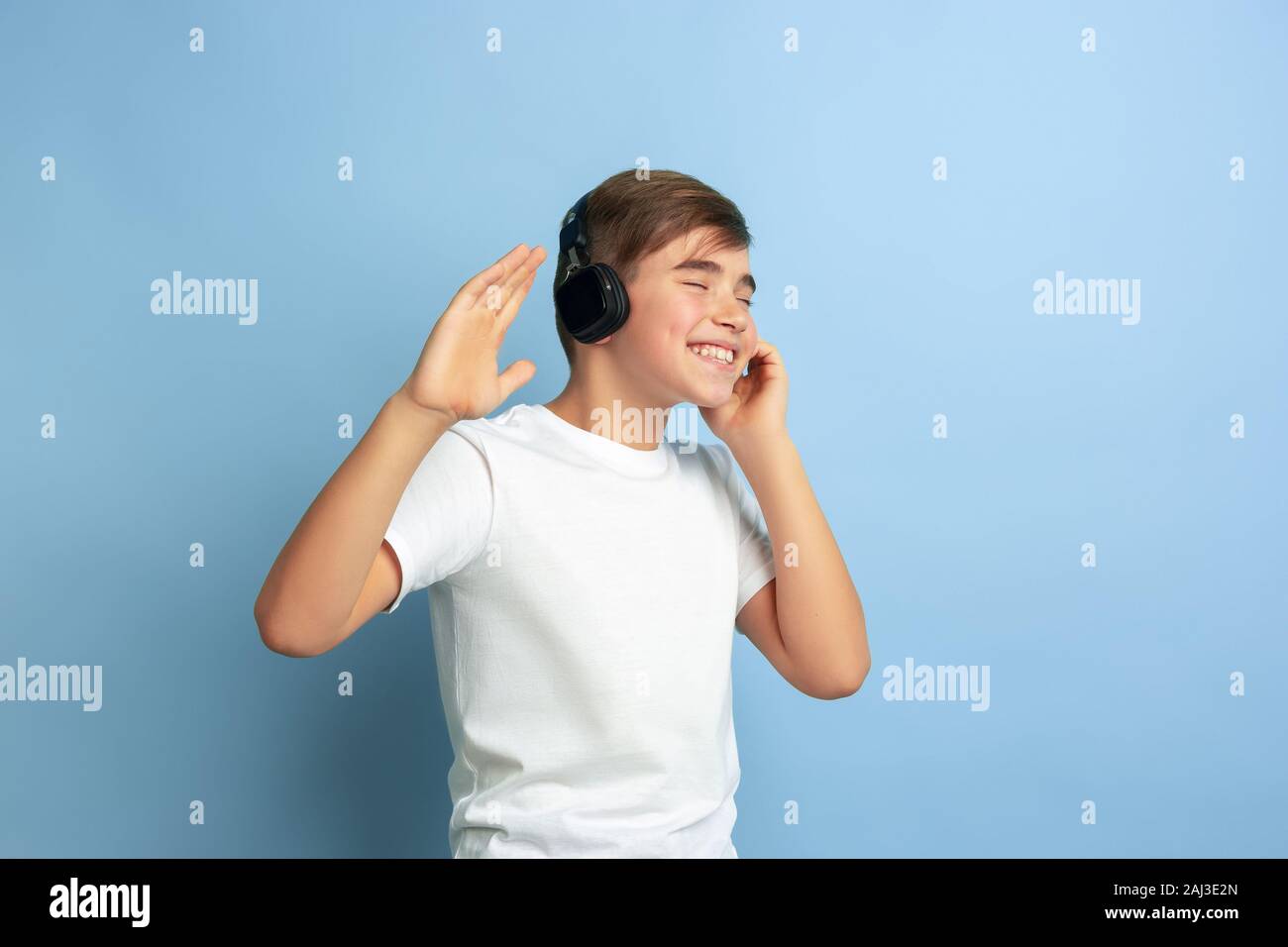 Listen to music, greeting. Caucasian boy portrait isolated on blue ...