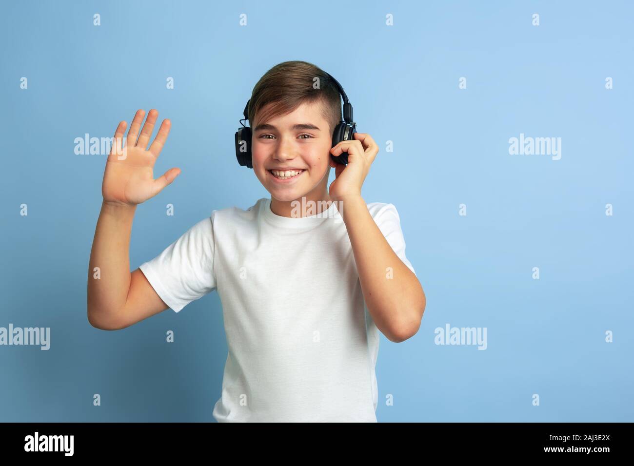Listen to music, greeting. Caucasian boy portrait isolated on blue ...