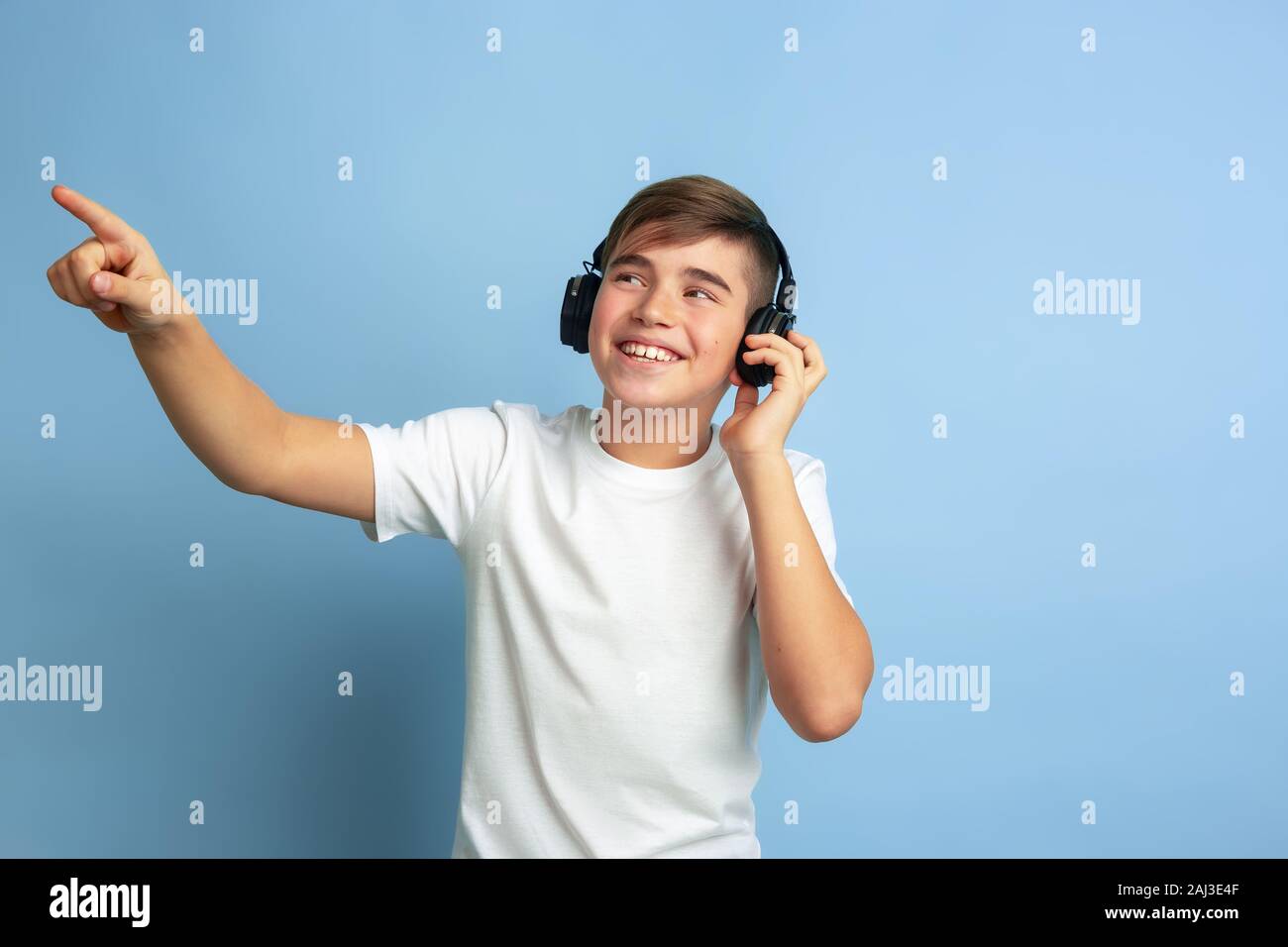 Listen to music, pointing at side. Caucasian boy portrait isolated on ...