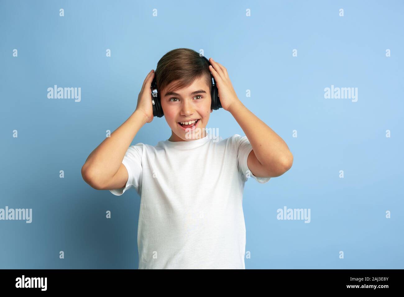 Listen to music, looks joyful. Caucasian boy portrait isolated on blue ...
